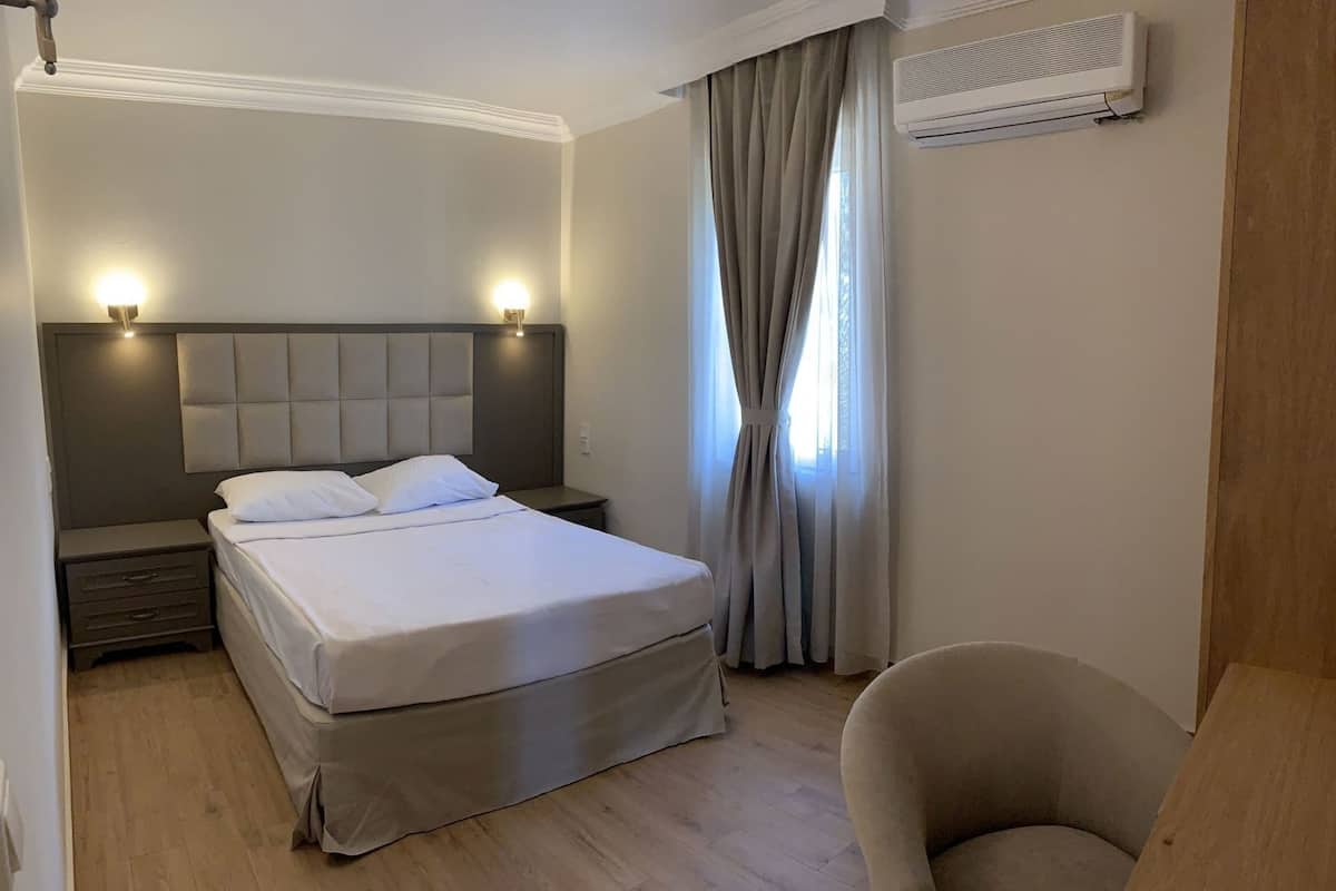 Quarto de hotel com cama, mesas de cabeceira, uma cadeira, ar condicionado e cortinas.