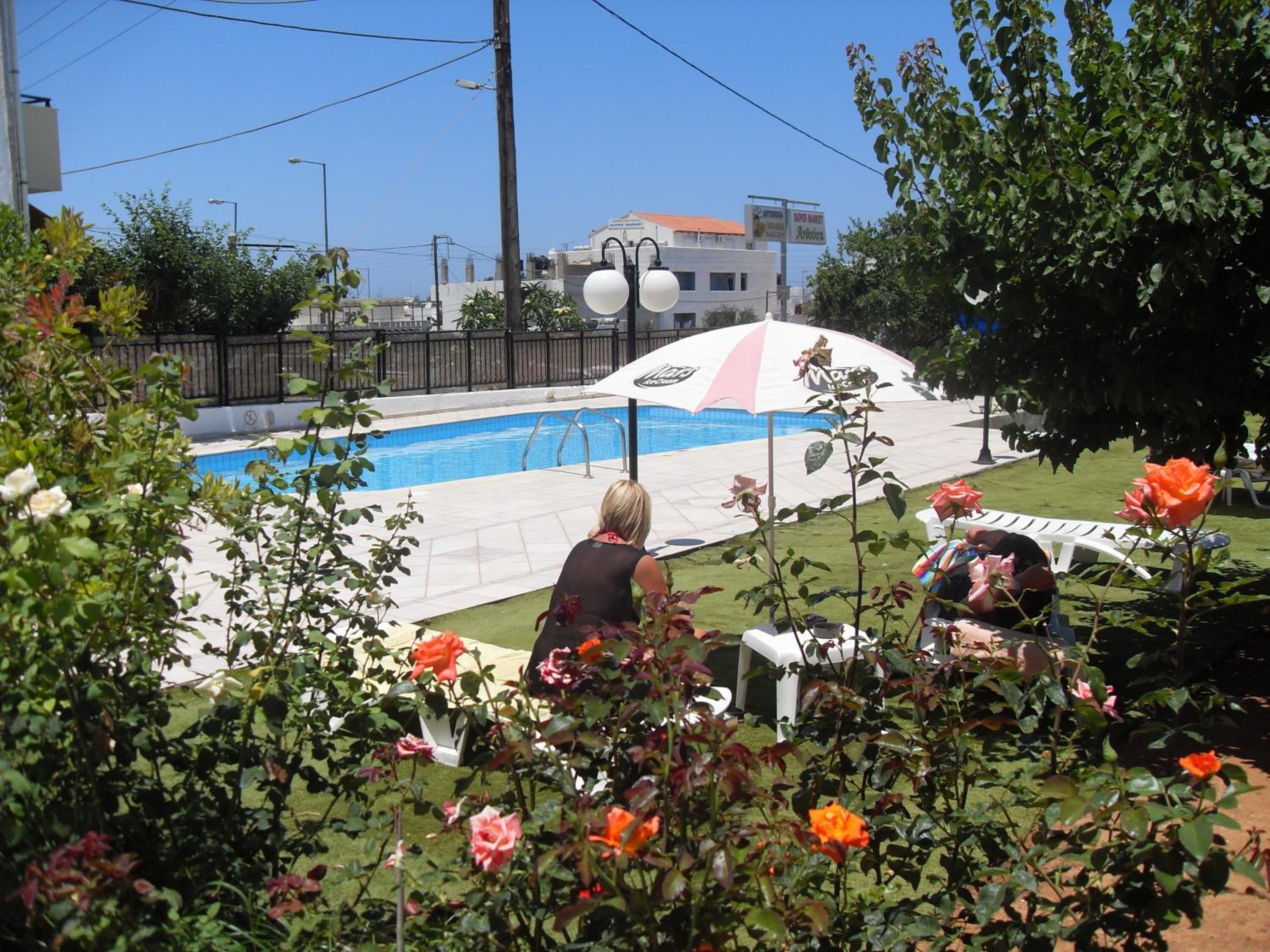 Piscina com guarda-sol branco, rodeada por vegetação e um muro.