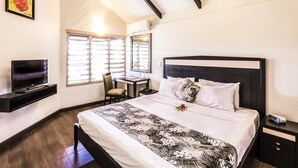 Quarto de hotel com cama, escrivaninha, televisão e janela com persianas.