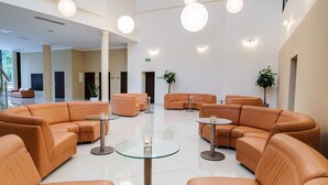 Um hall amplo com sofás de couro dispostos em semicírculo, uma mesa de centro de vidro no centro e iluminação pendente.