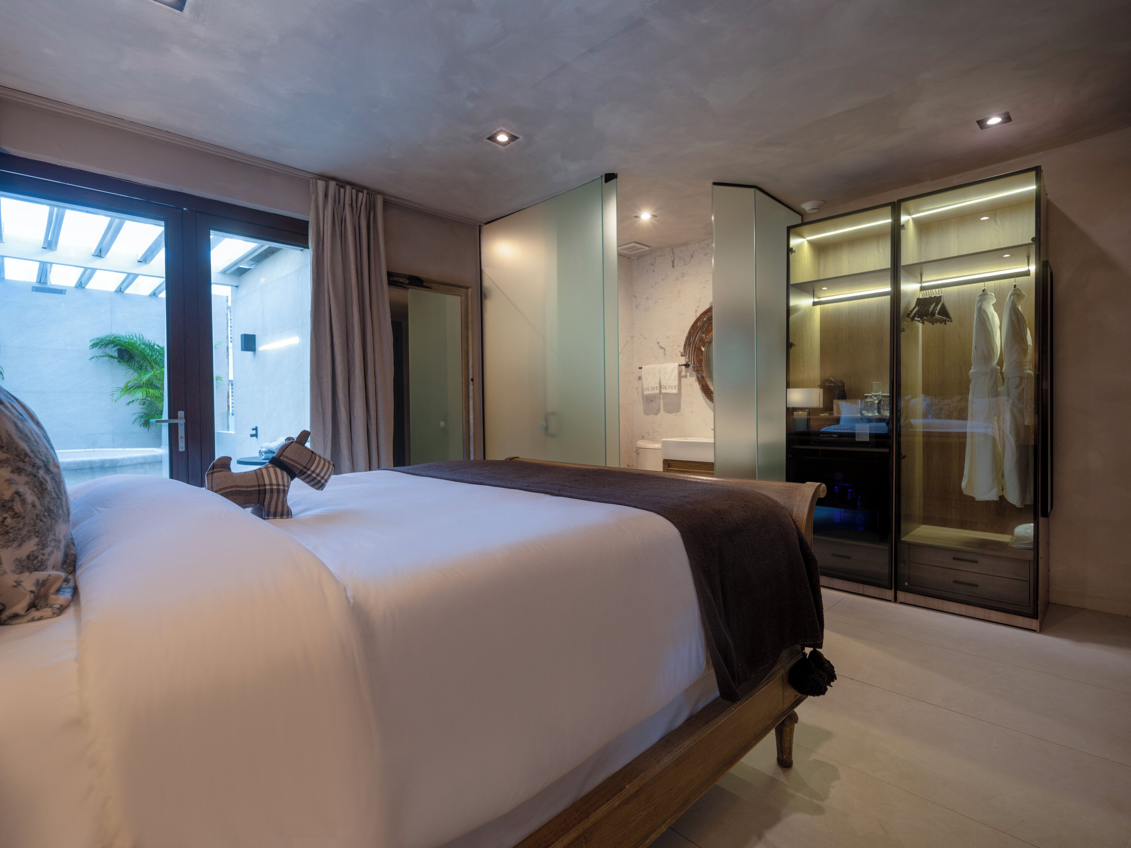 Quarto de hotel moderno com uma cama grande, um closet envidraçado e vista para o exterior.