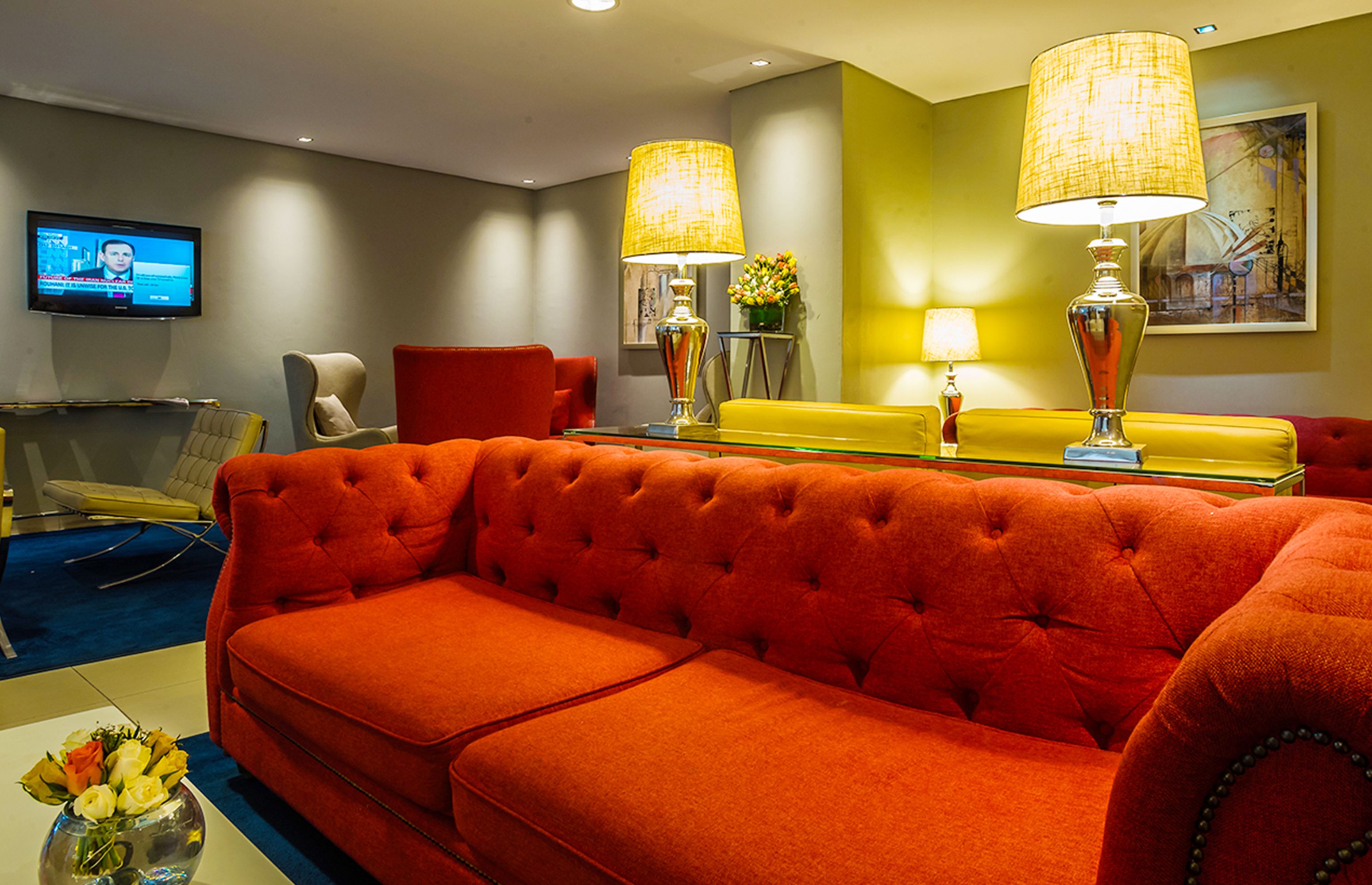 Uma sala de estar moderna com um sofá vermelho, duas luminárias, uma televisão e um vaso com flores.