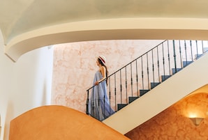 Uma mulher descendo uma escadaria curva com parede de mármore e corrimão preto.