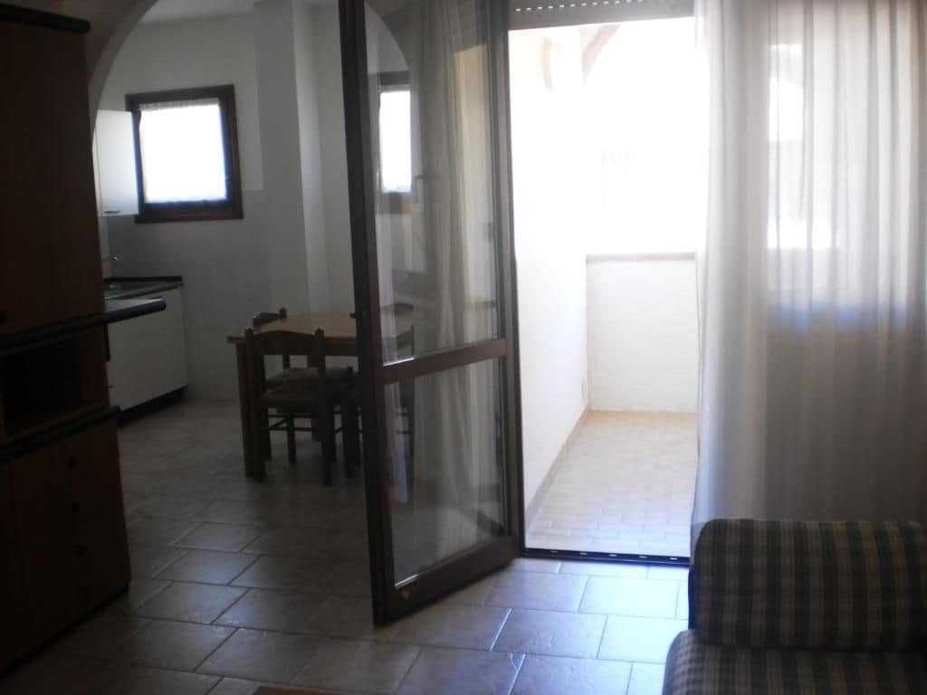 Um interior com porta de vidro deslizante para uma varanda, área de jantar com mesa e cadeiras, e um sofá.