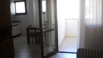 Um interior com porta de vidro deslizante para uma varanda, área de jantar com mesa e cadeiras, e um sofá.