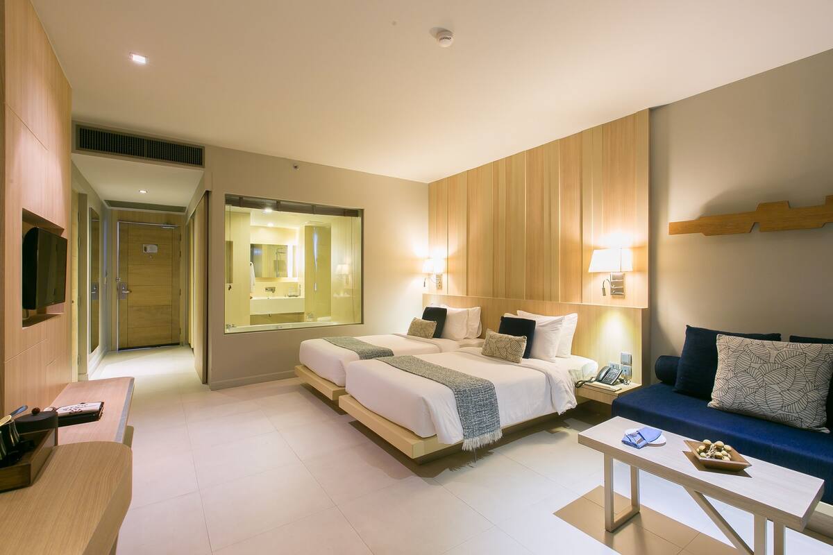 Quarto de hotel com duas camas, um sofá, uma escrivaninha e um espelho.
