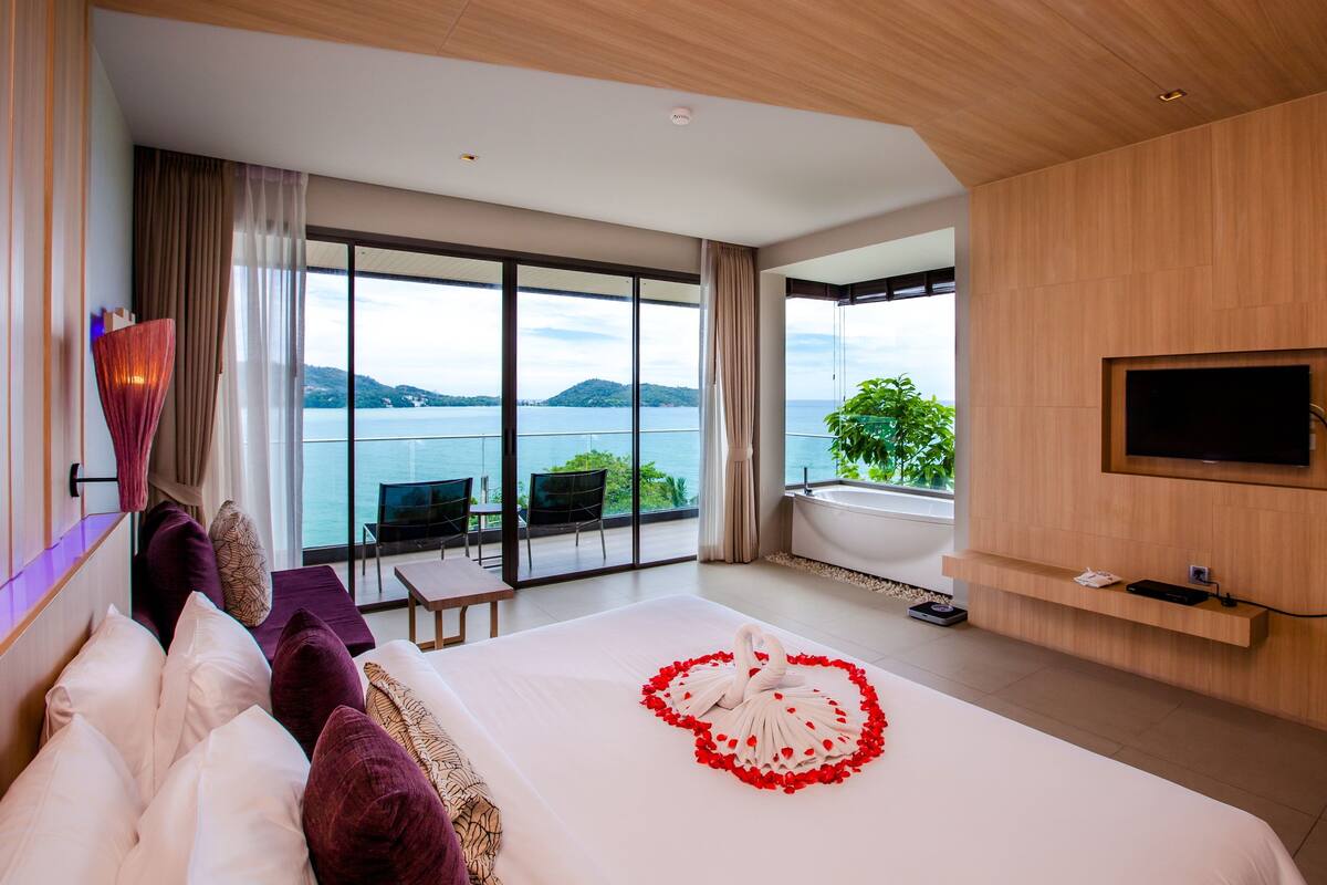 Quarto de hotel moderno com cama grande, televisão, banheira e varanda com vista para o mar.