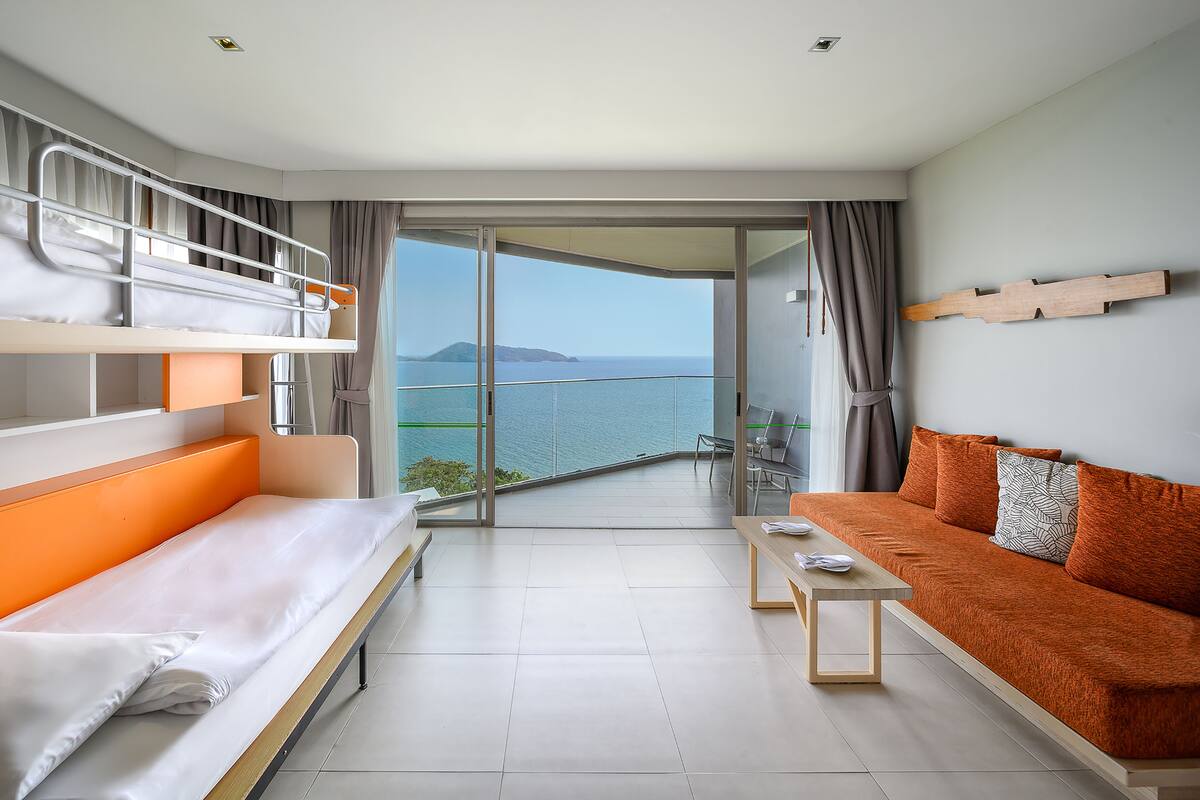 Quarto de hotel moderno com varanda, um sofá, uma cama e uma pequena mesa.