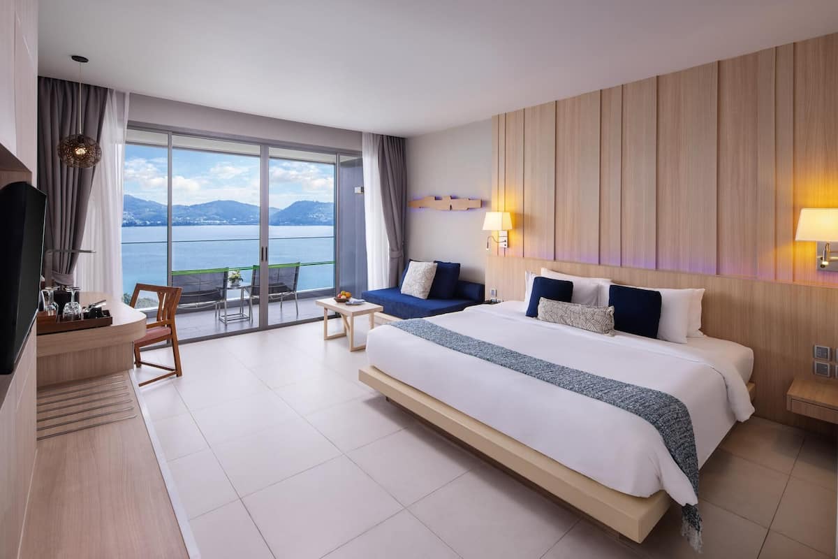 Quarto de hotel moderno com uma cama grande, uma escrivaninha, uma cadeira e varanda com vista para o mar.