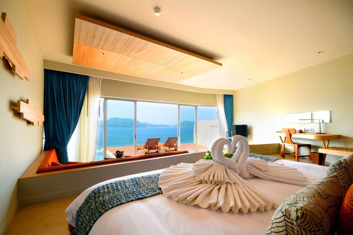 Quarto de hotel moderno com uma cama grande, uma escrivaninha e vista para o mar.