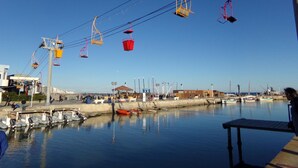 Uma área à beira-mar com um sistema de teleférico, barcos atracados e céu claro.