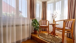 Um recanto acolhedor com um banco de madeira, cadeiras listradas, uma pequena mesa e um vaso com planta.