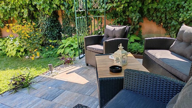 Um pátio com móveis de vime, um candeeiro e um jardim com diversas plantas.