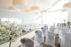 Decoração de cerimônia de casamento com cadeiras brancas, arranjo floral e luminárias pendentes grandes.
