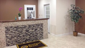 Uma área de recepção com parede revestida de azulejos, um balcão com computador e uma planta.