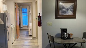 Quarto de hotel com área de jantar, cozinha equipada, extintor de incêndio e quadro na parede.