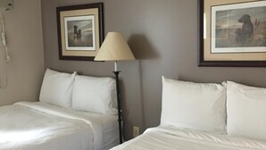 Quarto de hotel com duas camas de solteiro, uma mesa de cabeceira com abajur e dois quadros na parede.