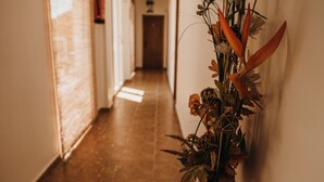 Um corredor com um arranjo floral na parede direita, piso de madeira e uma porta ao fundo.