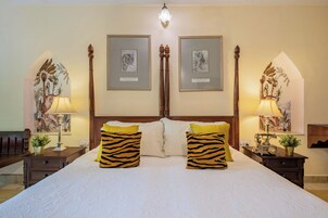 Uma cama grande com duas almofadas estampadas de tigre, uma cabeceira de madeira e duas molduras na parede.