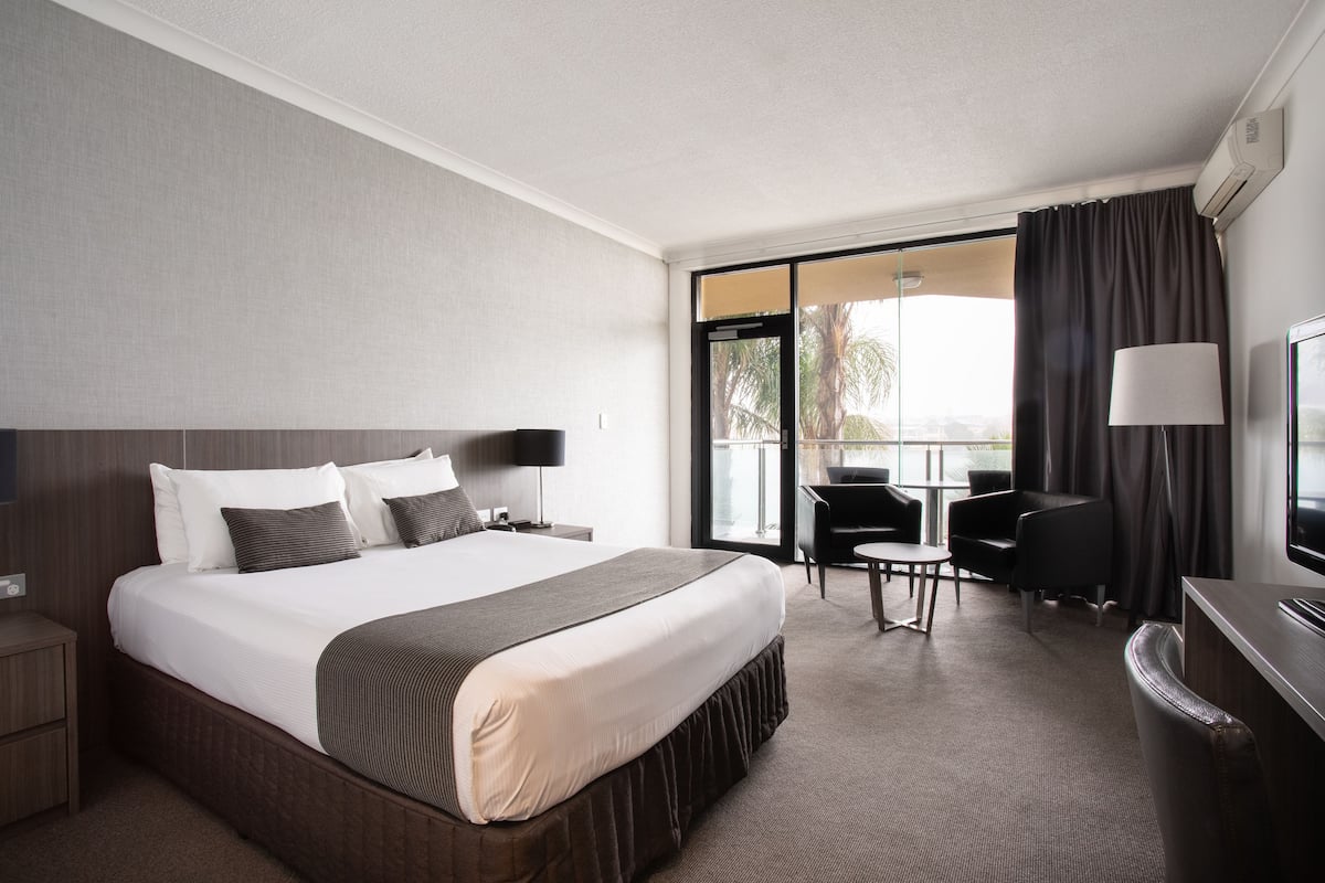 Quarto de hotel com uma cama grande, uma escrivaninha com cadeira, TV e varanda com vista.