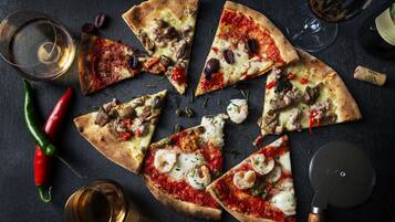 Pizza com diversos ingredientes, uma taça de vinho e um saca-rolhas sobre uma superfície escura.