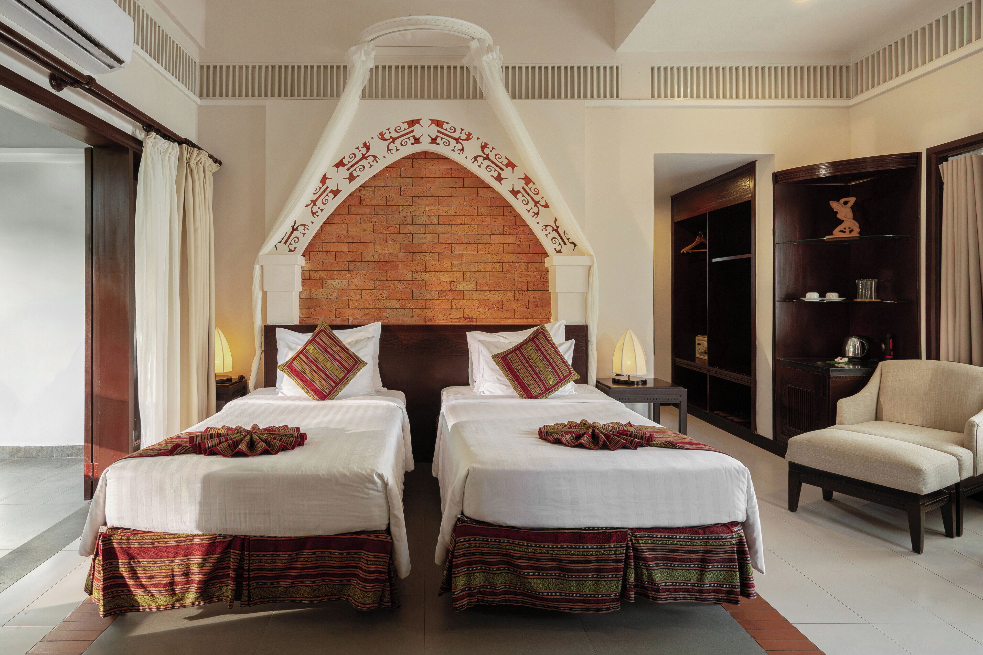 Quarto de hotel com duas camas, lareira de tijolos, guarda-roupa de madeira e uma cadeira.