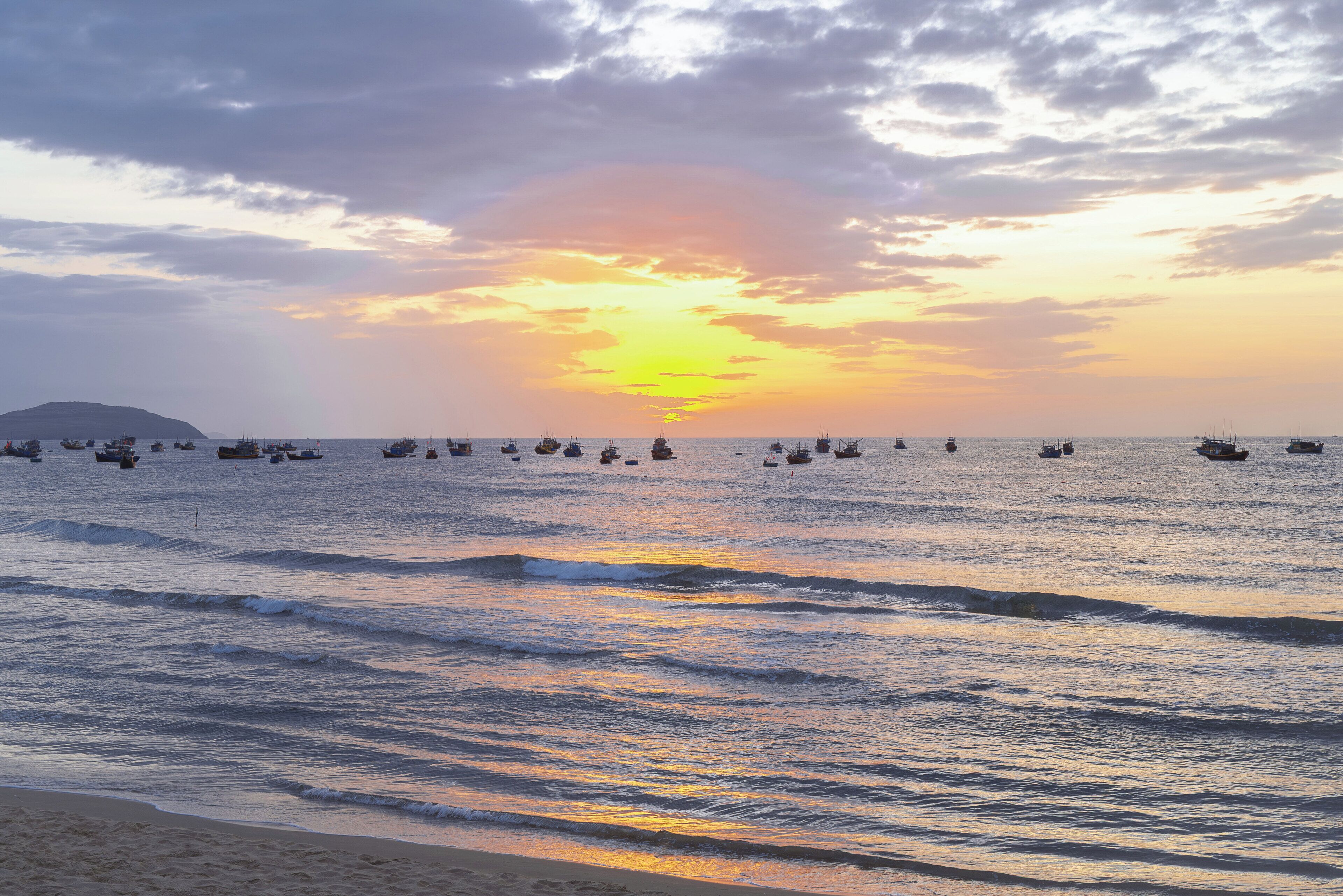 Uma praia com barcos e um pôr do sol.