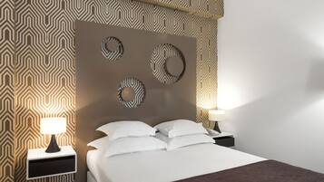 Um quarto moderno com papel de parede estampado, uma cama grande com lençóis brancos, duas mesas de cabeceira com luminárias e um ornamento circular na parede.