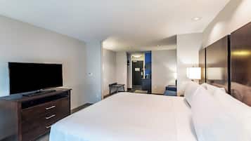 Quarto de hotel com uma cama grande, uma televisão de tela plana em uma cômoda de madeira, uma escrivaninha com cadeira e um espelho na parede.