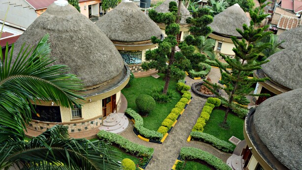 Um pátio com edifícios de telhado de palha, jardins bem cuidados e um elemento central de água.