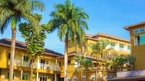 Hotel de vários andares com varandas, palmeiras e um céu azul límpido.