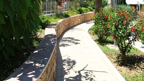 Um caminho de pedra sinuoso, ladeado por vegetação exuberante e palmeiras, conduz a um edifício com sacadas.