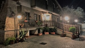 Um edifício de pedra com varanda, plantas em vasos e um pátio pavimentado.