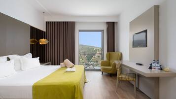 Quarto de hotel com cama, escrivaninha, cadeira, janela com vista e televisão na parede.