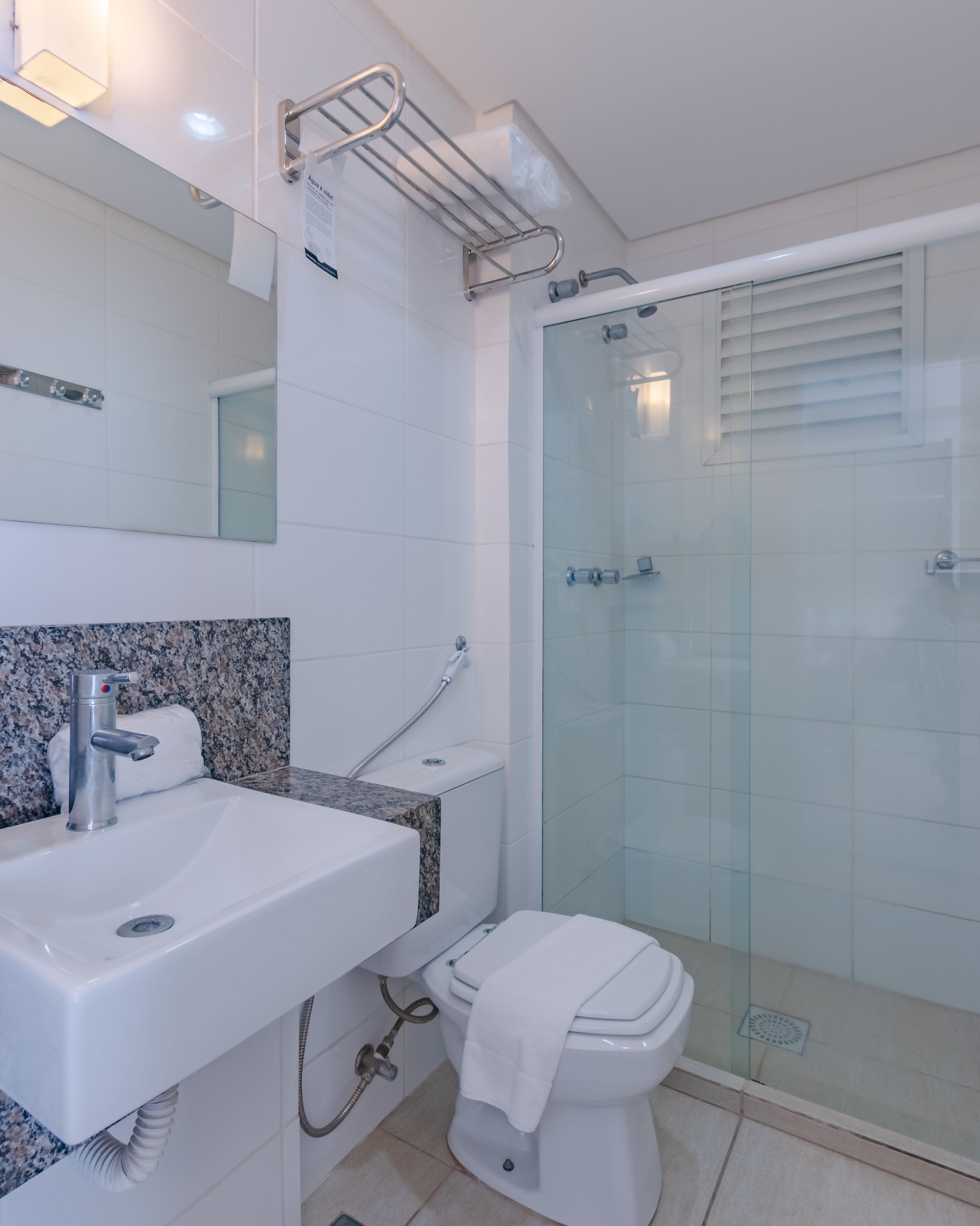Casa de banho moderna com lavatório branco, bancada de granito e cabine de duche em vidro.