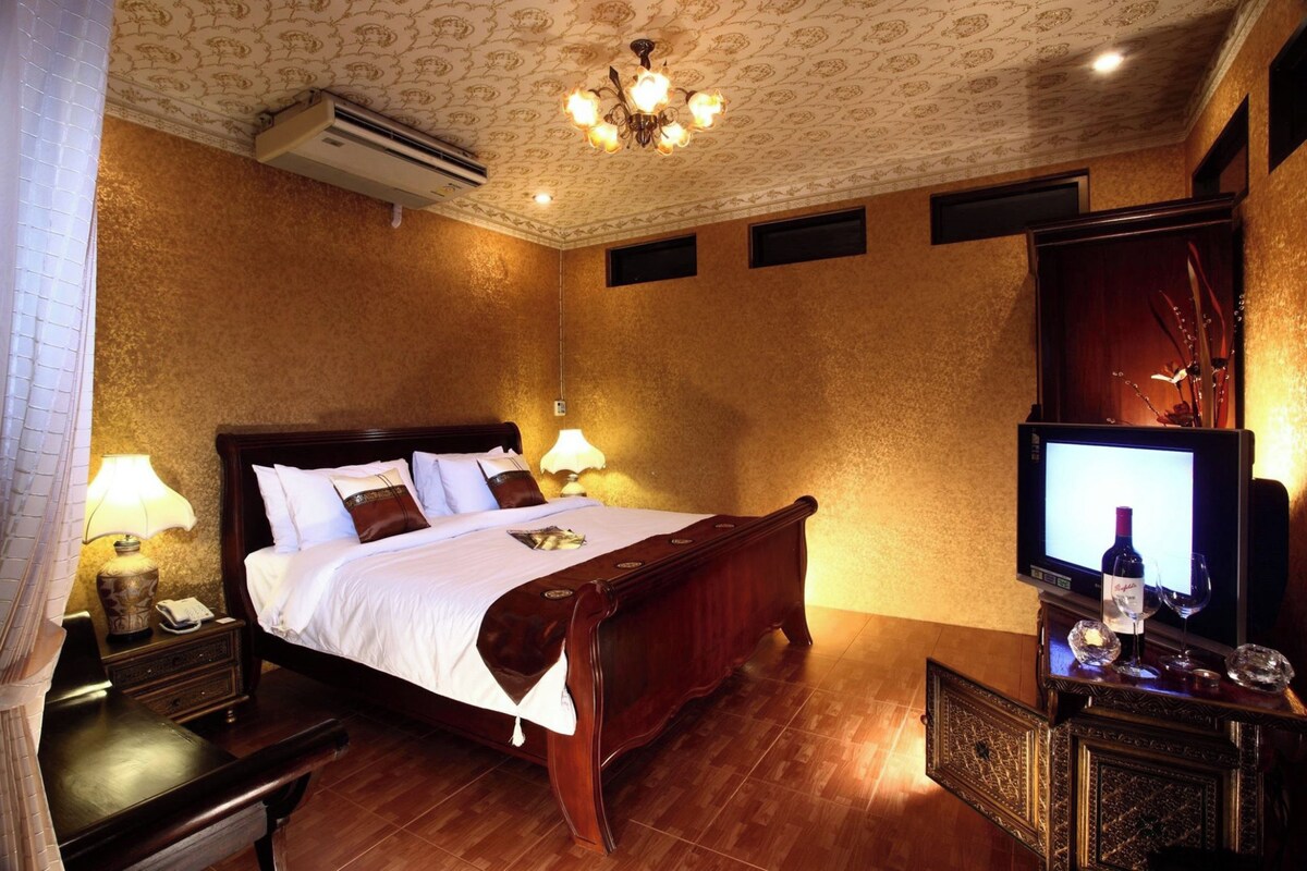 Quarto de hotel com cama de madeira, abajures, televisão e minibar.