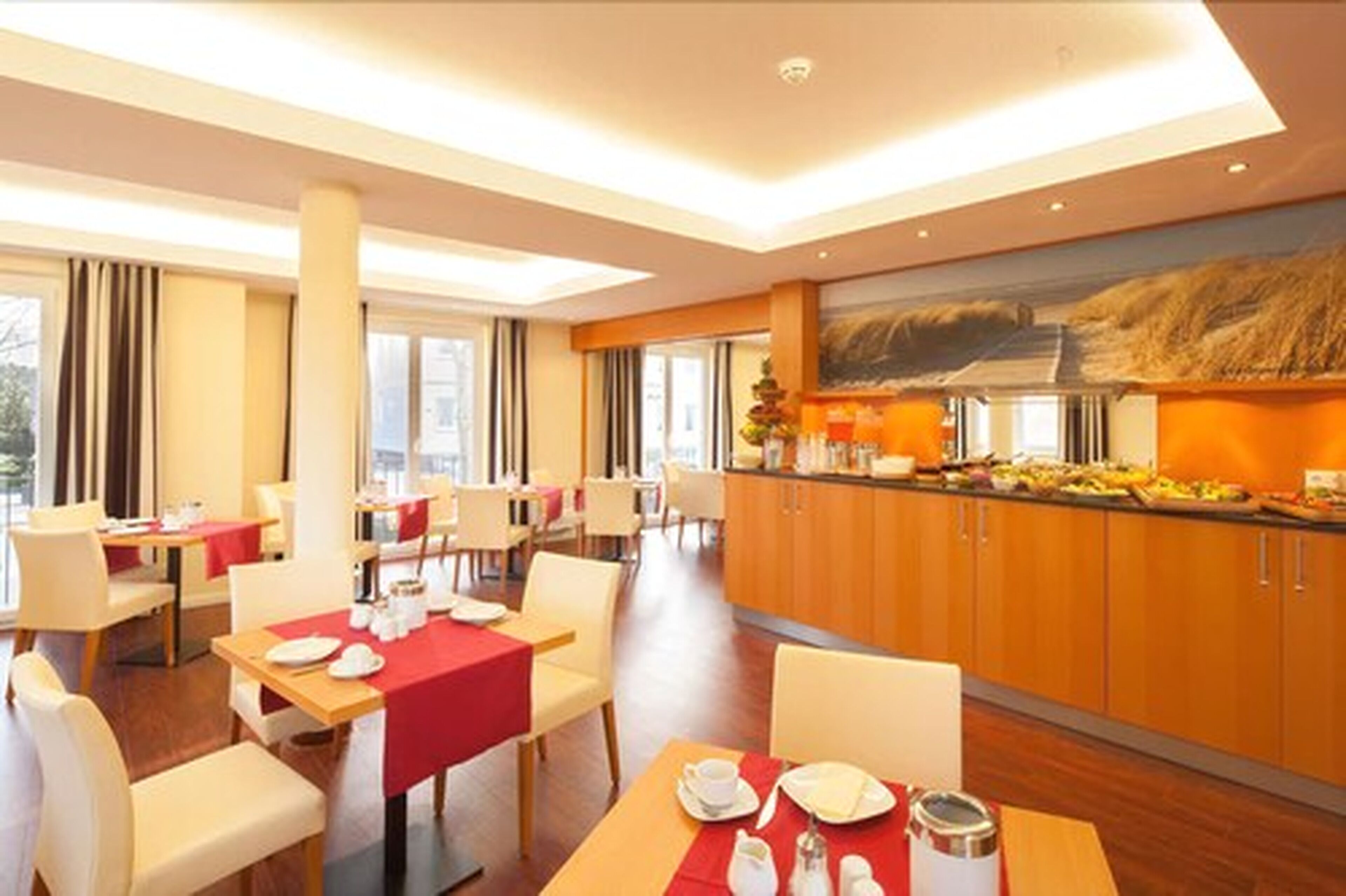 Uma área de jantar moderna com mesas preparadas para o café da manhã, um balcão de buffet e uma grande janela com vista para a cidade.