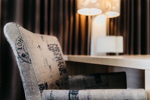 Um close-up de uma cadeira de estilo vintage com padrão em tecido, uma mesa de madeira e uma luminária ao fundo.