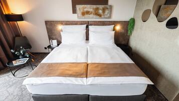 Uma cama de casal com cabeceira, mesa de cabeceira com abajur e uma revista sobre ela.