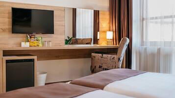 Quarto de hotel com cama, secretária com televisão de tela plana, cadeira, abajur e janela com cortinas.