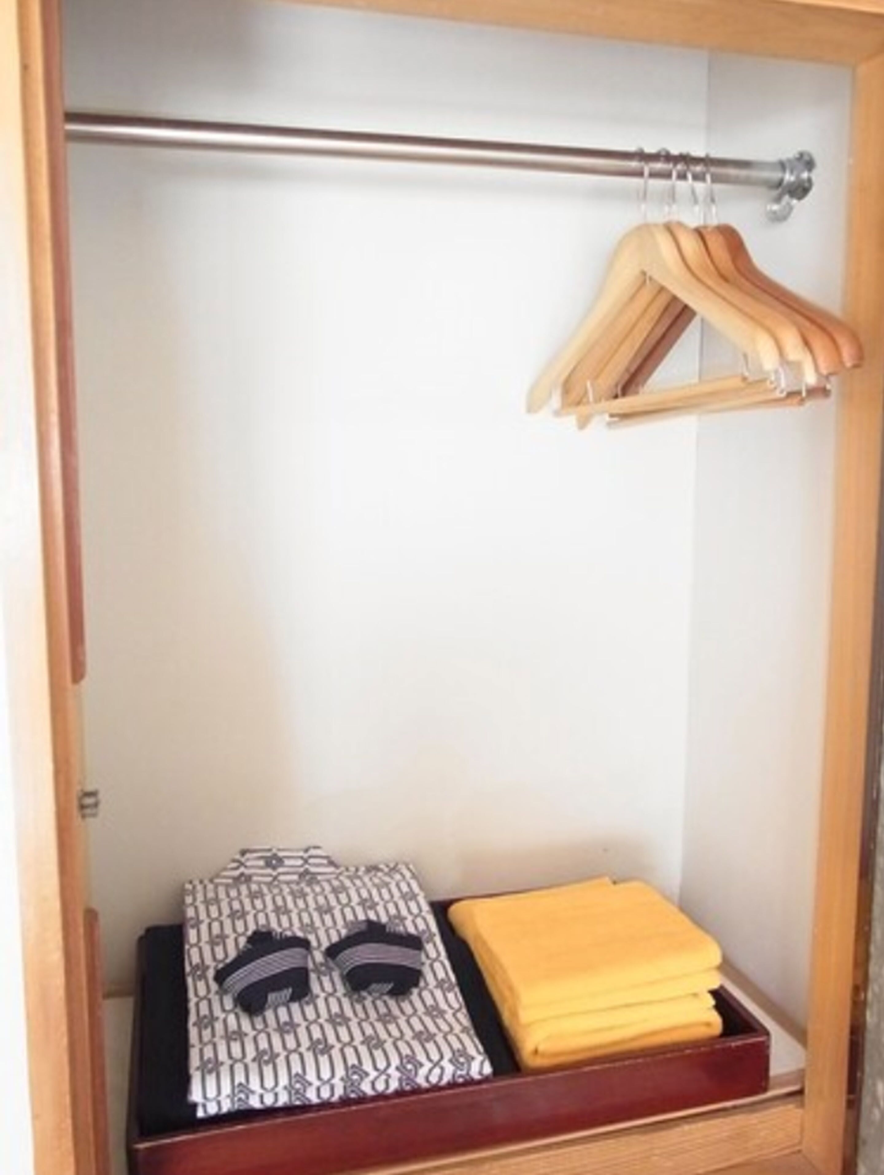 Um guarda-roupa com barra para pendurar e prateleira com roupas dobradas e um par de sapatos.