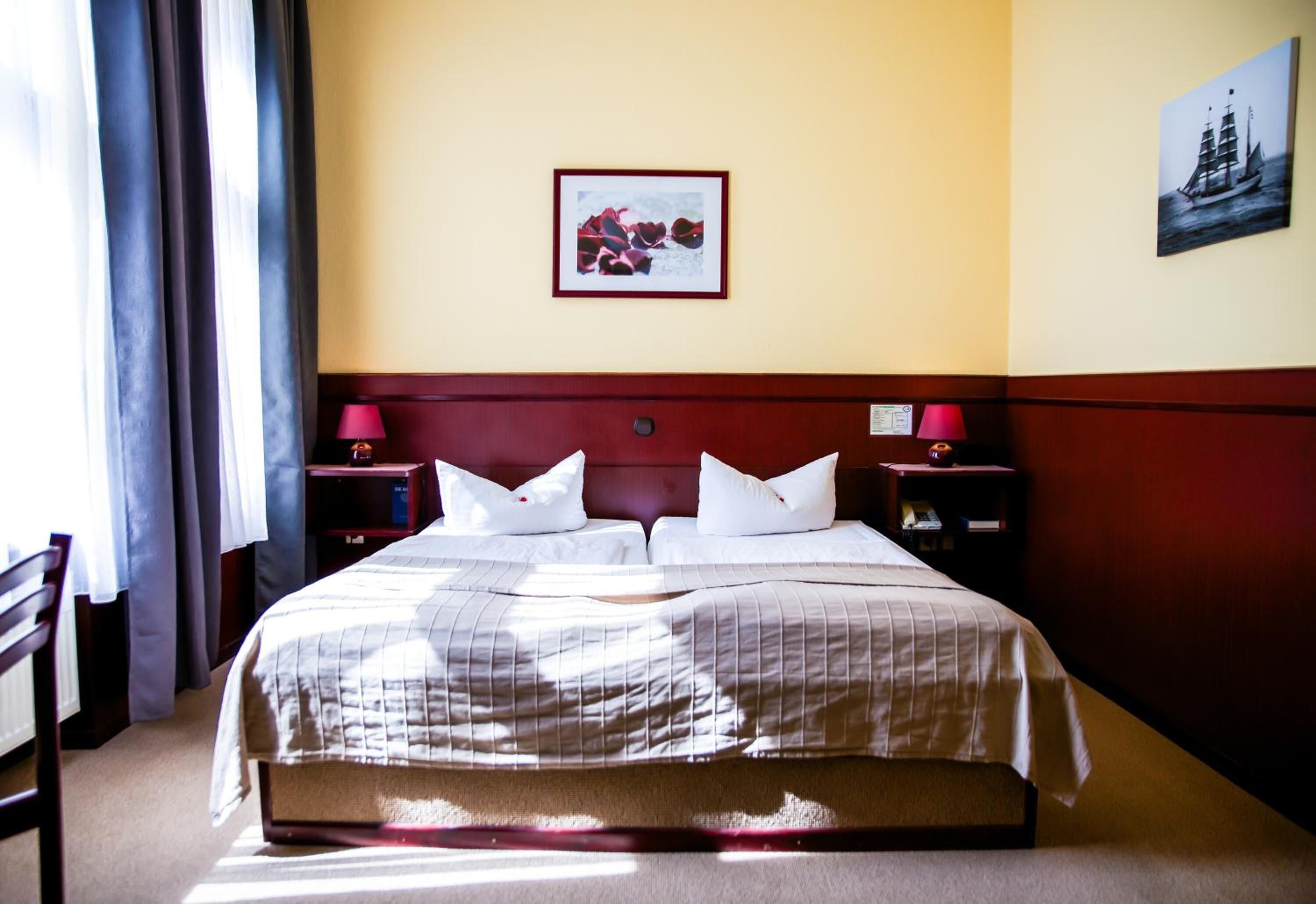 Quarto de hotel com uma cama grande, duas mesas de cabeceira com luminárias, um quadro na parede e uma janela com cortinas.