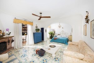 Uma sala de estar ampla com lareira, um sofá azul, uma poltrona branca e piso estampado.