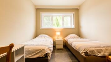 Quarto pequeno e bem iluminado com duas camas de solteiro, mesa de cabeceira e escrivaninha.