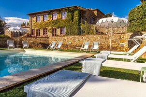 Um edifício de pedra com piscina, cadeiras de descanso brancas e guarda-sóis.