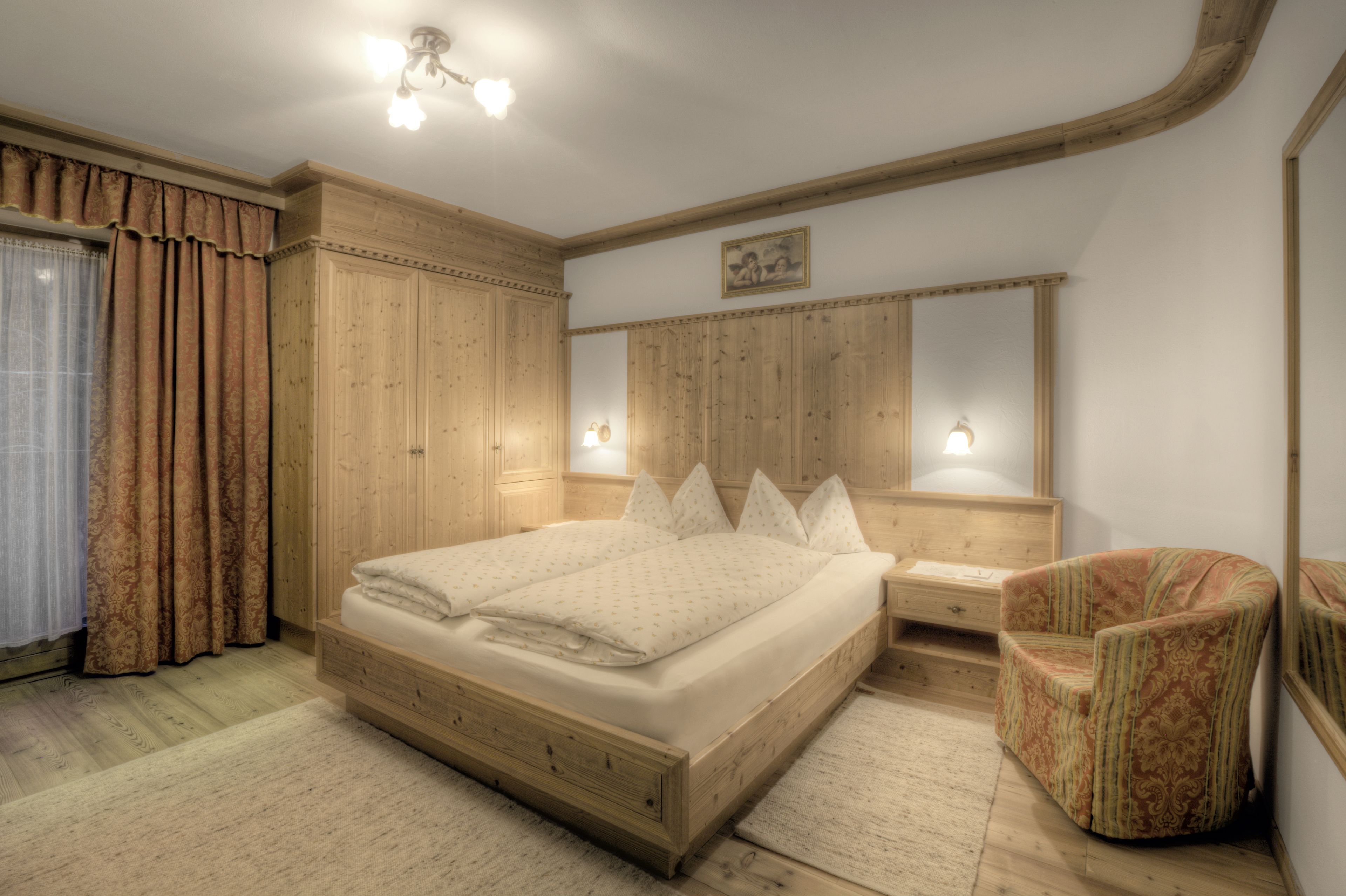 Quarto com cama de madeira, mesa de cabeceira, cadeira e espelho.