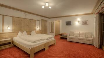Quarto com cama de madeira, um sofá, mesa de cabeceira e televisão fixada na parede.