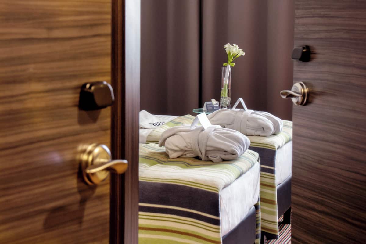 Quarto de hotel com duas camas, um vaso com flores e uma cama bem arrumada com um cobertor listrado.