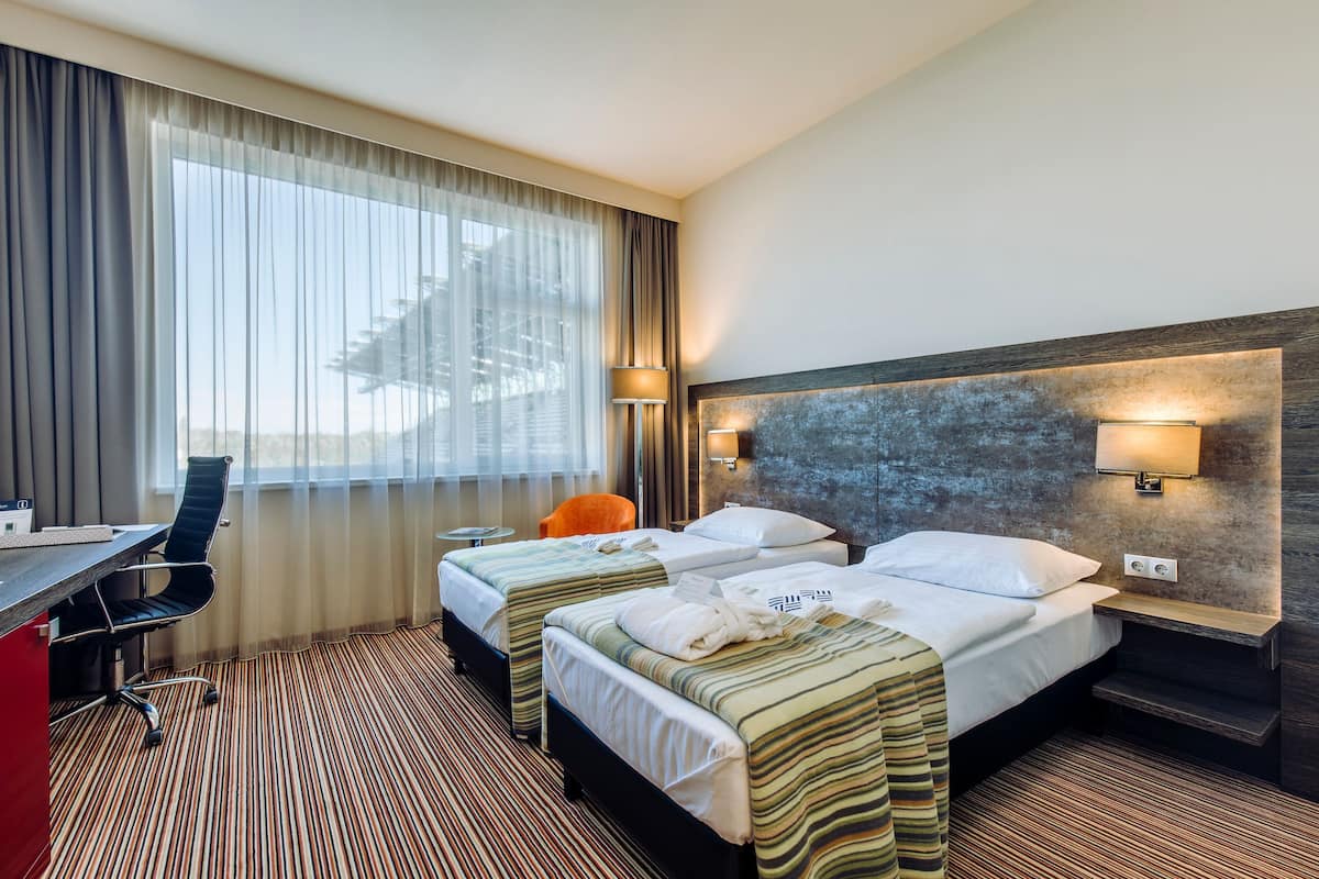 Quarto de hotel com duas camas, uma escrivaninha e uma cadeira.