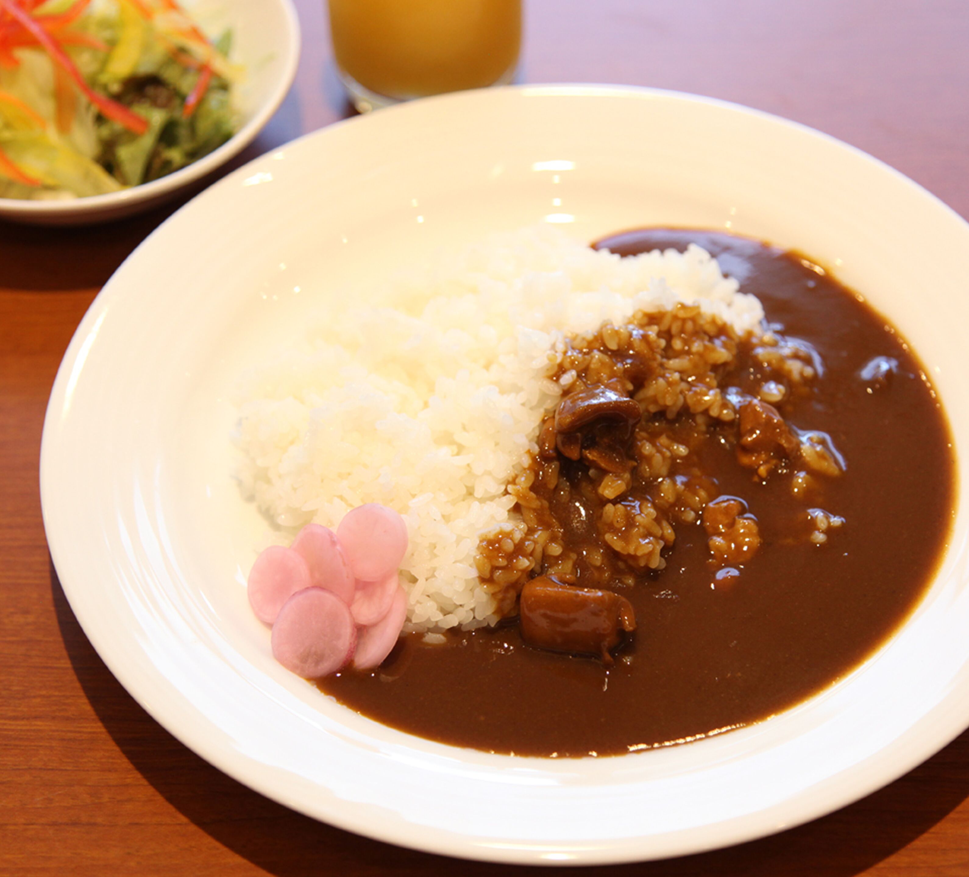 Um prato de arroz branco com molho marrom e acompanhamentos em conserva cor-de-rosa, servido em um prato branco.